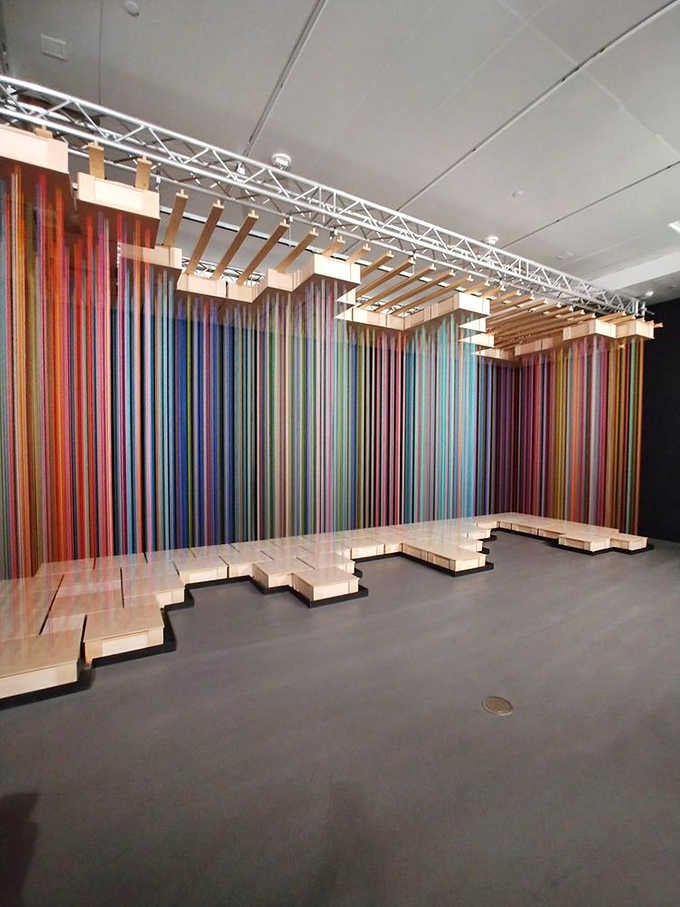 Rainbow ribbons cascade like a waterfall of pure joy frozen mid-splash against the gallery wall.