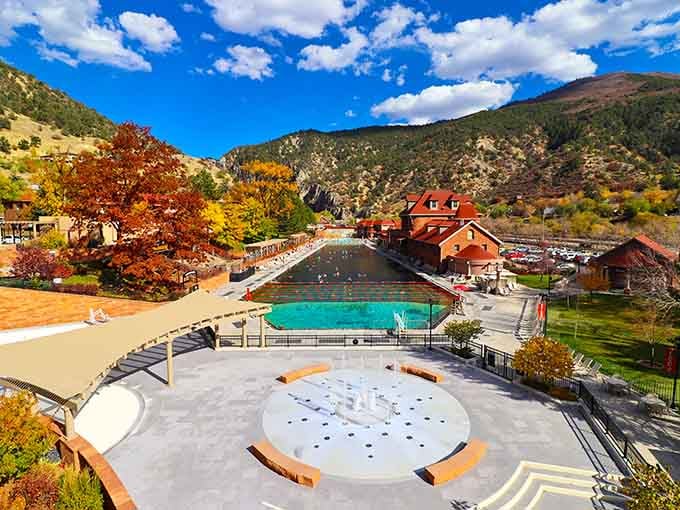 The massive thermal pool stretches endlessly while fall colors paint the surrounding mountains in nature's most vibrant autumn palette.