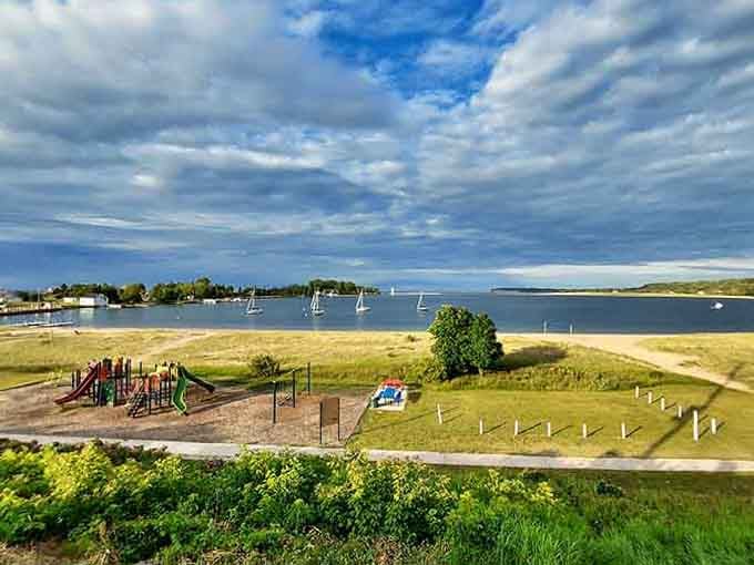 Sailboats dot the protected harbor while dramatic clouds paint the sky in shades of blue and silver.