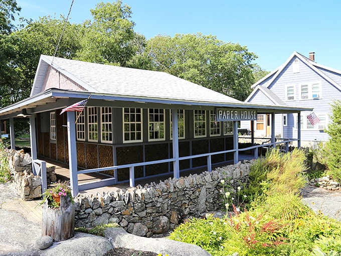 This quirky cottage wrapped in porch railings sits surrounded by colorful gardens, looking charmingly eccentric against the coastal landscape.