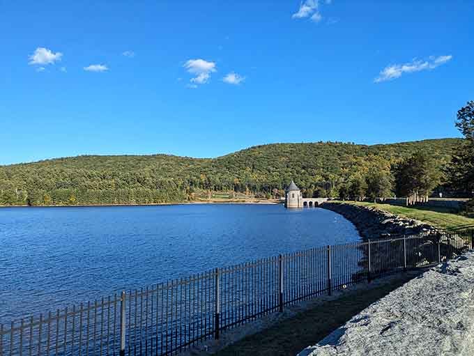The reservoir stretches peacefully beneath rolling hills, its calm surface reflecting clouds like a giant mirror of sky.