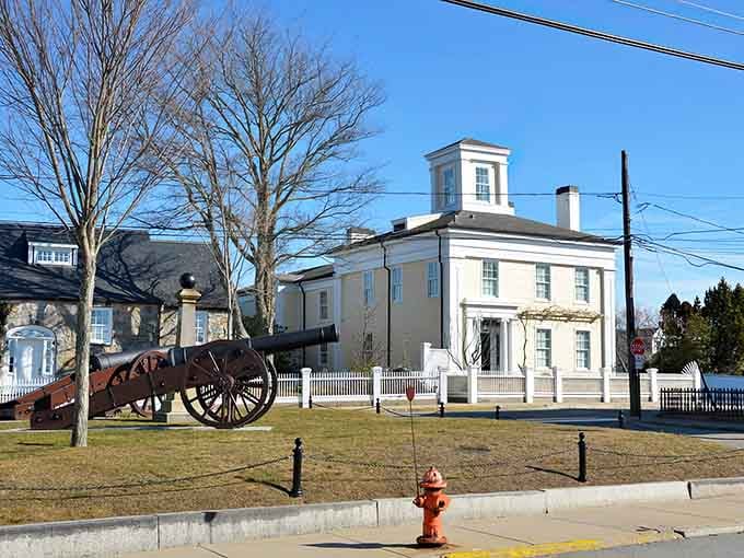 Stonington's classic white building with cupola sits beside a historic cannon, blending Revolutionary War history with everyday New England life.