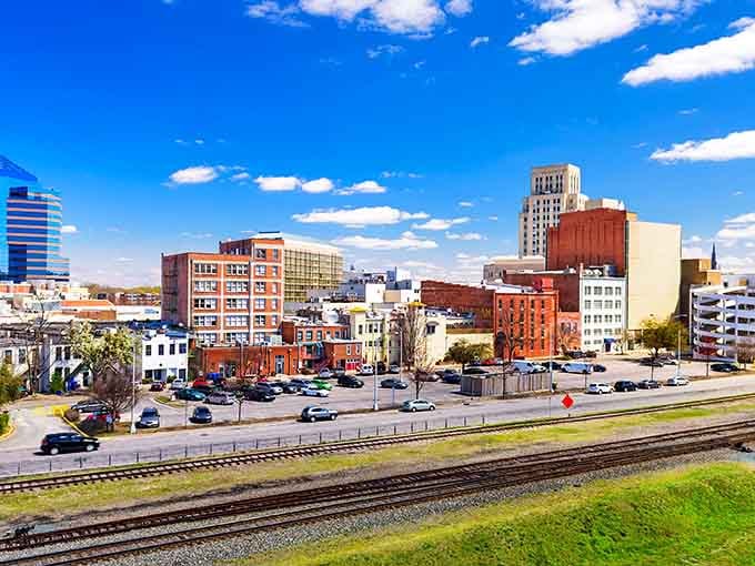 Railroad tracks cut through the urban landscape where brick warehouses stand shoulder-to-shoulder with modern towers under endless blue skies.