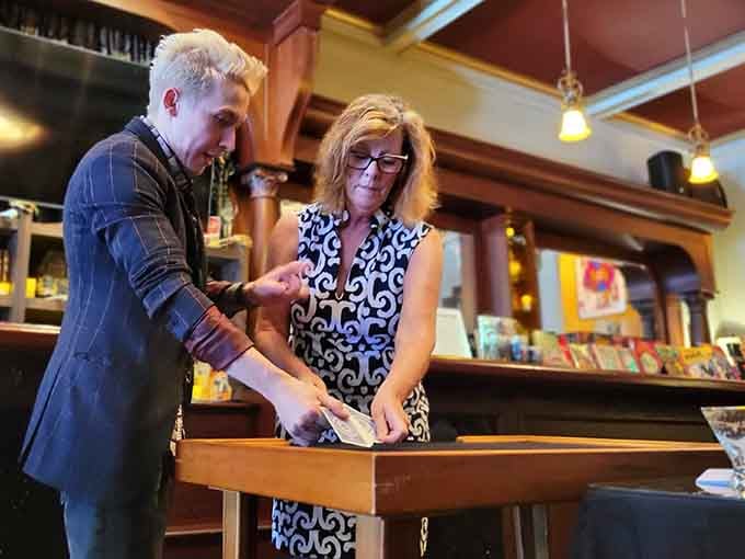 The magician's focused hands work their craft while guests lean in, captivated by sleight-of-hand artistry and wonder.