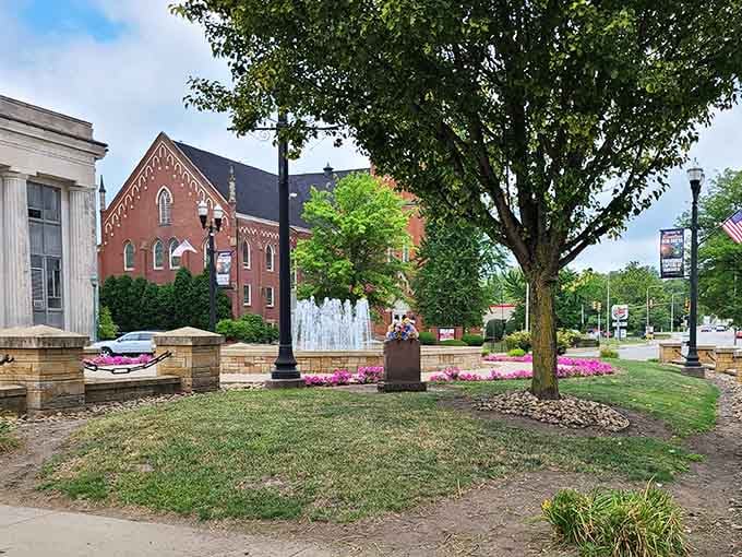 Fountains and flowers frame historic buildings in a town square that looks ready for a summer concert or community gathering.