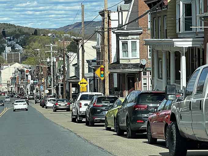 Mountains rise behind main street where parked cars and power lines prove small-town life still thrives in Pennsylvania's valleys.