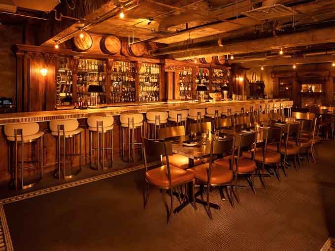 The bar stretches like a golden promise, backed by enough bottles to make any cocktail dream come true.