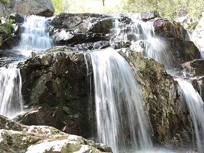 Water cascades over ancient volcanic rock in multiple tiers, creating Missouri's own natural masterpiece worth the hike.
