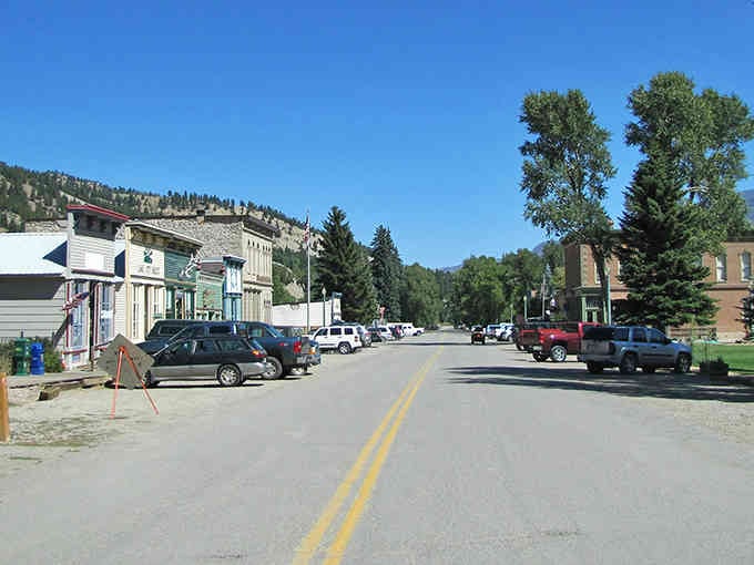 Lake City's charming main street showcases colorful historic buildings nestled against towering mountain slopes under brilliant blue Colorado skies.