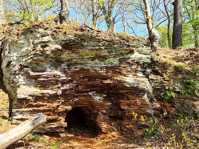 Ancient, layered rock formations reveal a small hidden cave nestled among the trees, inviting explorers to discover nature's quiet wonders.