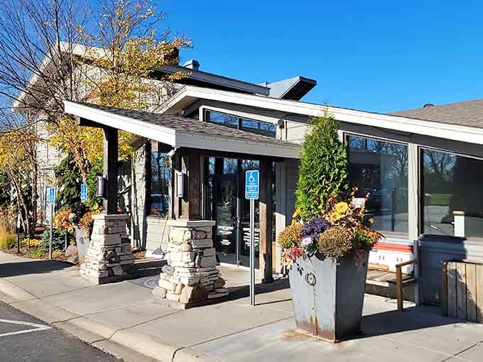 Stone pillars and autumn blooms frame the entrance where lakeside dining dreams begin on a perfect blue-sky day.