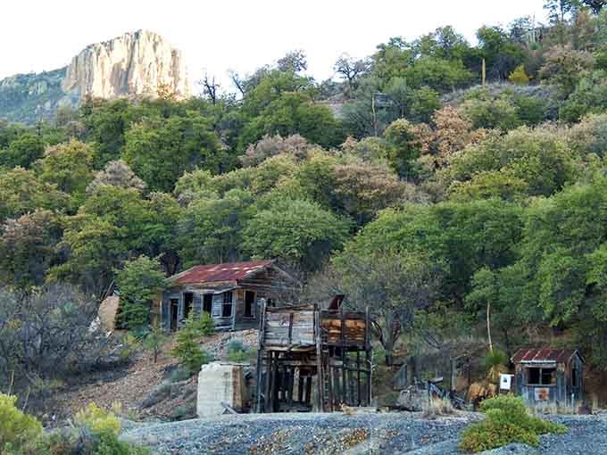 Nature's reclaiming what miners built, with dramatic cliffs watching over weathered structures like silent sentinels of history.