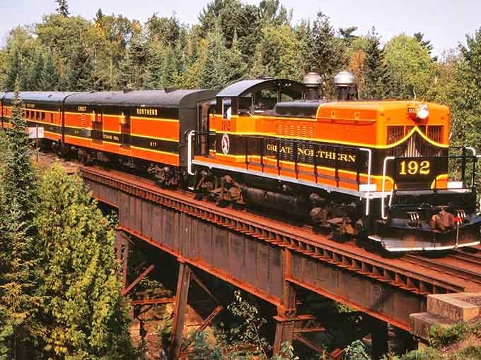 That brilliant orange and black locomotive crossing the trestle looks like autumn decided to become a train.