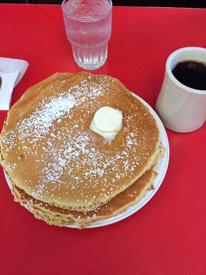 Pancakes dusted with powdered sugar and topped with butter are basically edible happiness on a red plate.