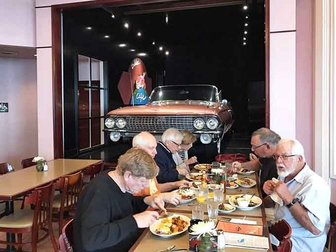 Diners enjoying their meals beneath a vintage Cadillac, because normal restaurant decor is overrated and boring anyway.