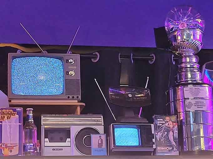 Vintage TVs displaying static, cassette players, and boom boxes create a museum of obsolete technology we somehow miss.