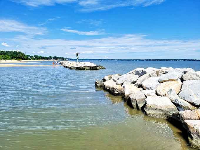 Rock breakwaters create calm swimming areas while sailboats dot the horizon like a postcard come to life.