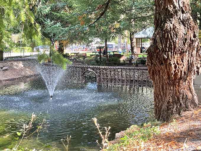 A fountain sprays in the park's pond while a miniature trestle bridge crosses overhead, doubling the charm factor.