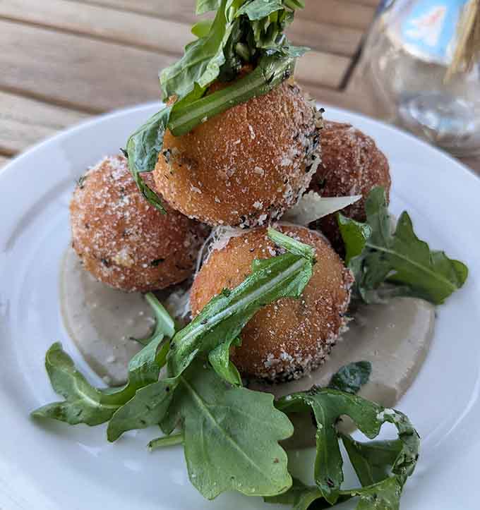 Golden arancini sitting pretty on a bed of greens, proving that fried rice balls are always a good idea, always.