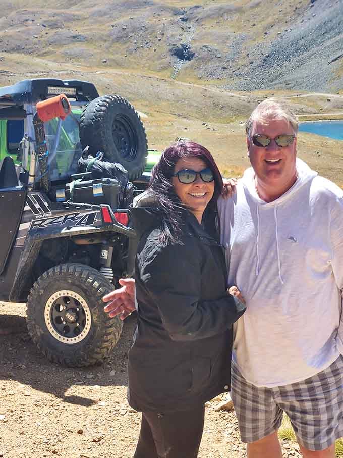 Happy visitors pause for photos, their smiles matching the stunning backdrop of alpine lakes below.