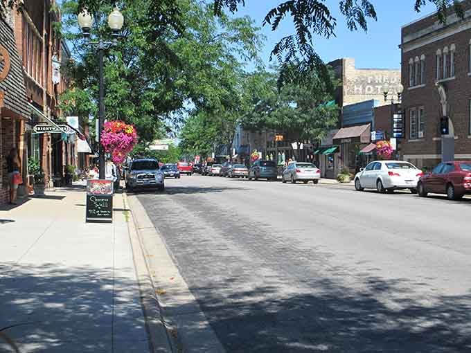 Summer flowers burst from hanging baskets while mature trees shade sidewalks perfect for window shopping and people-watching.