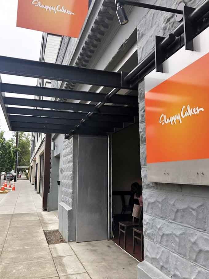 That cheerful orange signage and industrial-chic entrance hint at the delicious breakfast creativity happening behind those modern walls.