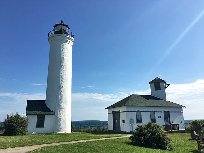 The lighthouse stands sentinel over the harbor, its white tower gleaming against endless blue sky.