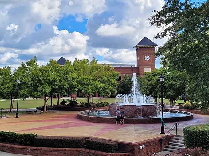 The fountain dances in front of brick buildings and clock tower, creating a peaceful gathering spot for the community.