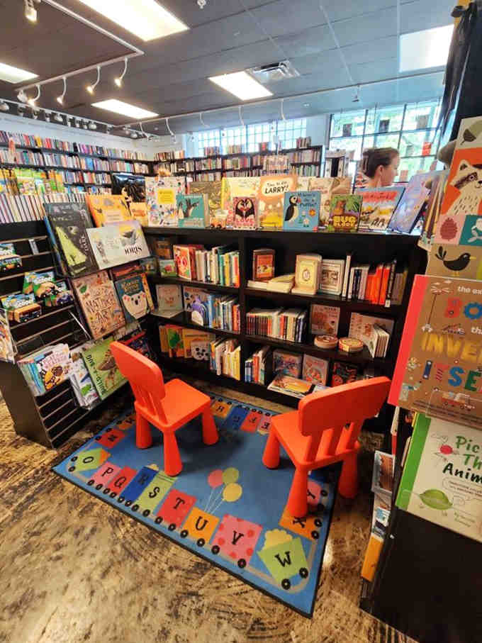 Bright orange chairs and colorful rugs create a welcoming kids' corner where young readers begin their literary journeys.