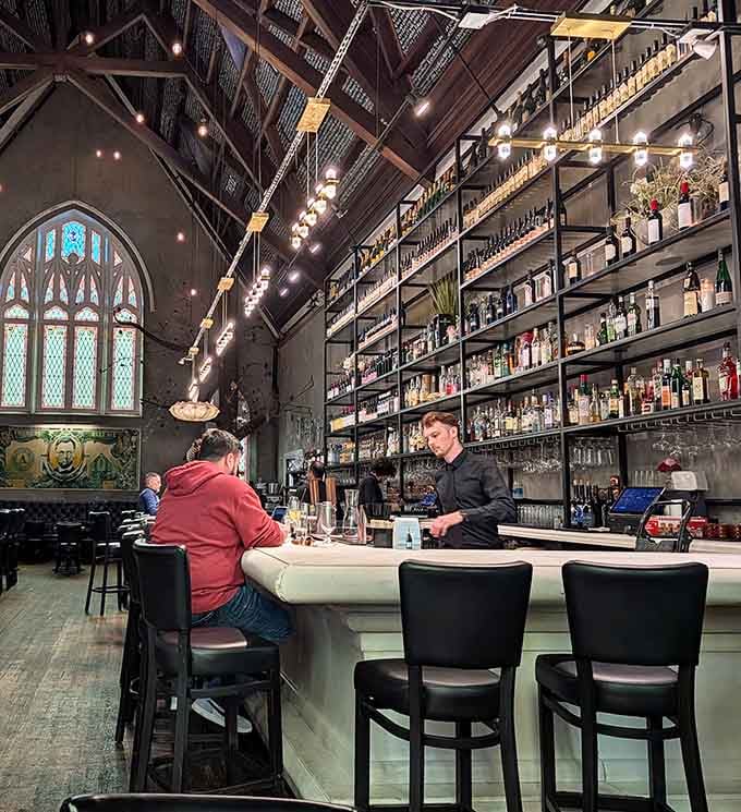 The towering bar shelves reach toward heaven while the stained glass windows cast colorful light across patrons enjoying their cocktails.