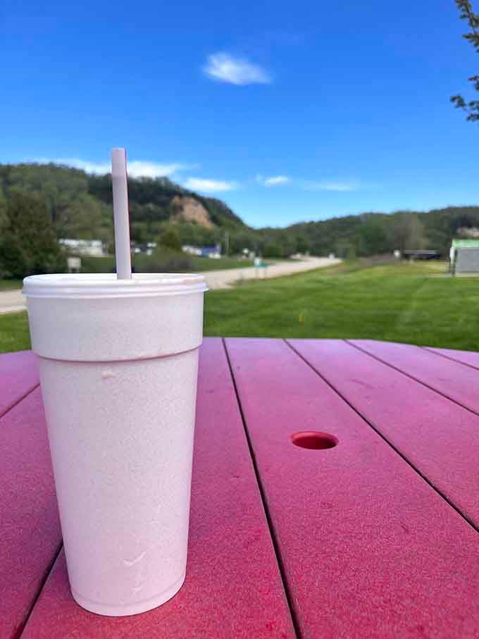A frosty beverage on a red picnic table with rolling hills beyond is peak Wisconsin summer dining experience.