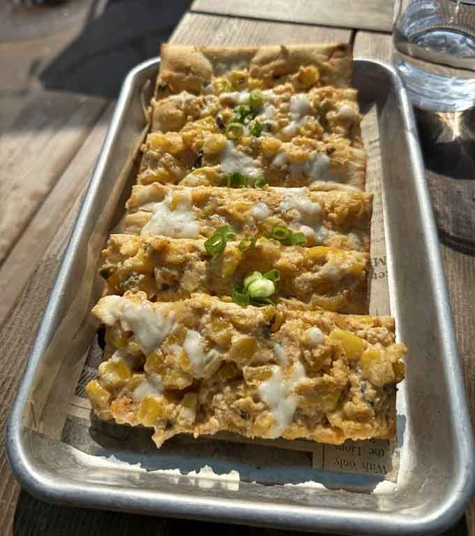 Crispy flatbread loaded with sweet corn and drizzled cheese proves vegetarian options can steal the whole dang show.