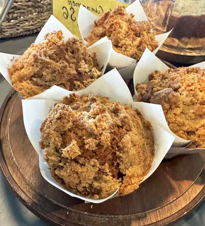 Peach crumble muffins with that perfect golden-brown top that makes you want to order one for now and three for later.