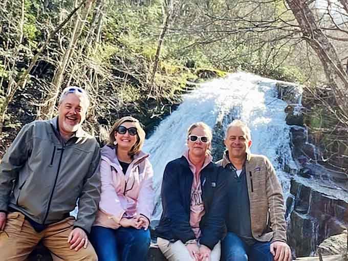 Four happy hikers proving that waterfalls are the universal language of outdoor joy and family bonding.