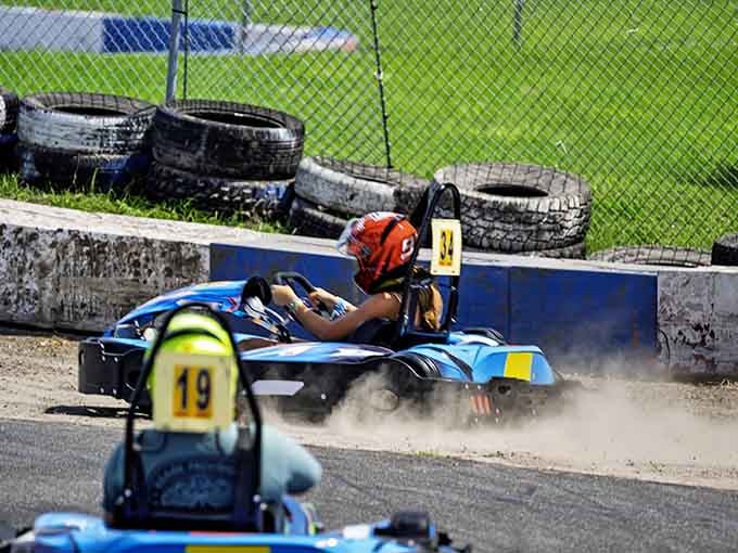 Gravel sprays dramatically as the driver wrestles through a challenging corner, demonstrating why karting demands real athletic skill.