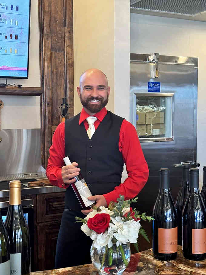 That genuine smile and professional presentation suggest someone who actually enjoys sharing great wine with curious visitors daily.