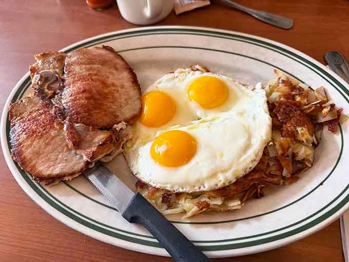 Three perfectly fried eggs crowning a generous pork chop and hash browns, because sometimes breakfast needs to be taken seriously.