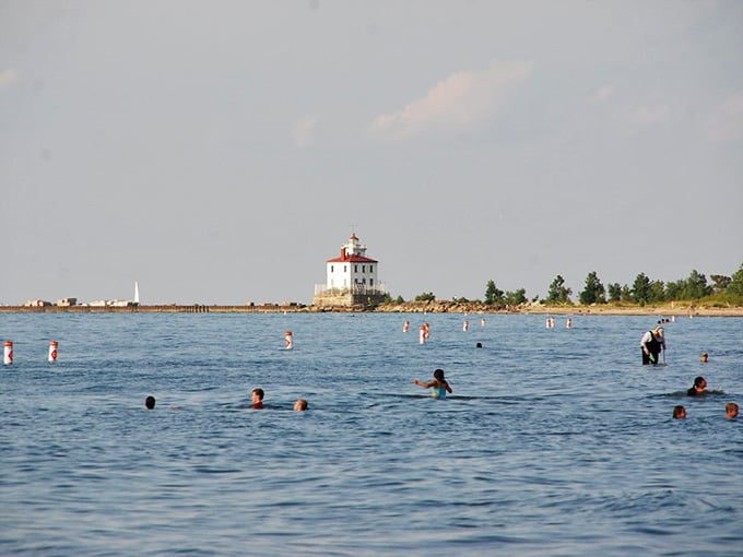 Swimmers splash near the historic lighthouse, enjoying refreshing lake waters under skies that seem to go on forever.