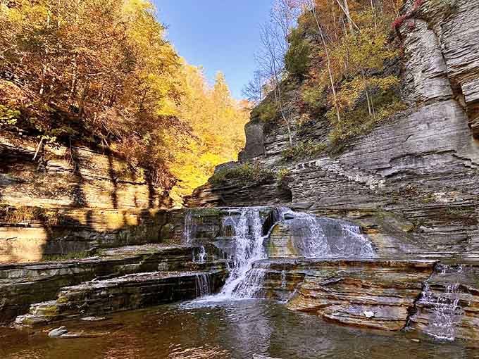 Golden autumn light illuminates the layered waterfall as it cascades into mirror-smooth pools below.