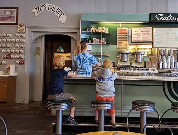 Two young customers demonstrate the proper counter-sitting technique, proving good taste transcends generations and reaches new heights literally.