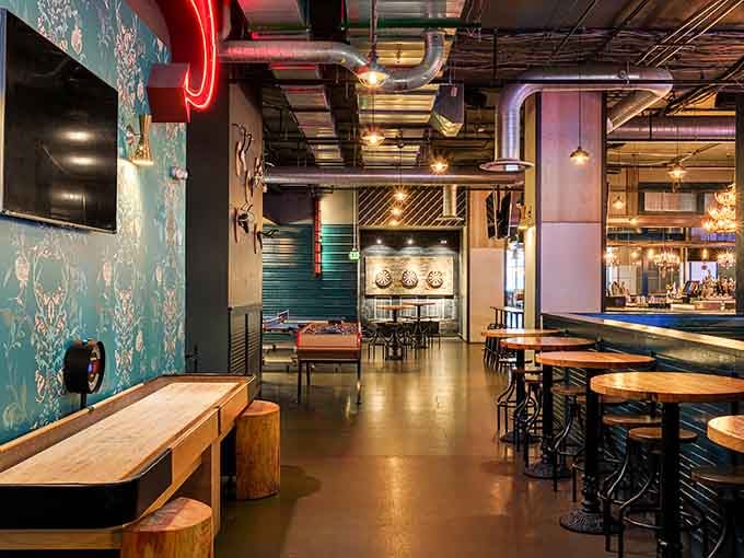 Shuffleboard lanes stretch beneath eclectic decor, blending nostalgia with contemporary design throughout the multilevel space.