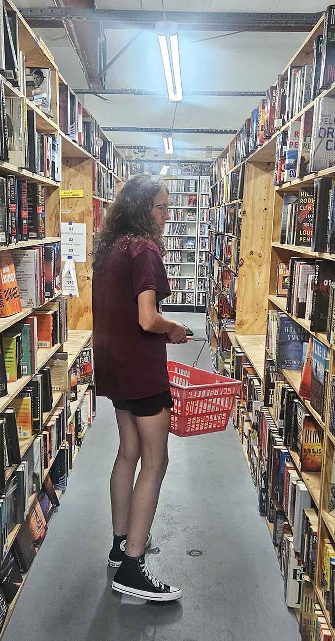 Fellow treasure hunters navigate the aisles with red baskets, already plotting where these books will live on their shelves.