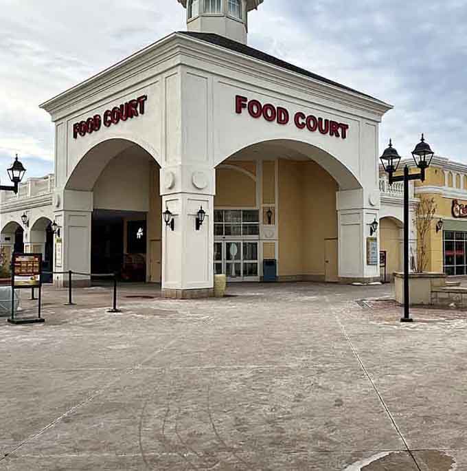 The food court entrance beckons weary shoppers with the promise of sustenance and air-conditioned relief from retail warfare.