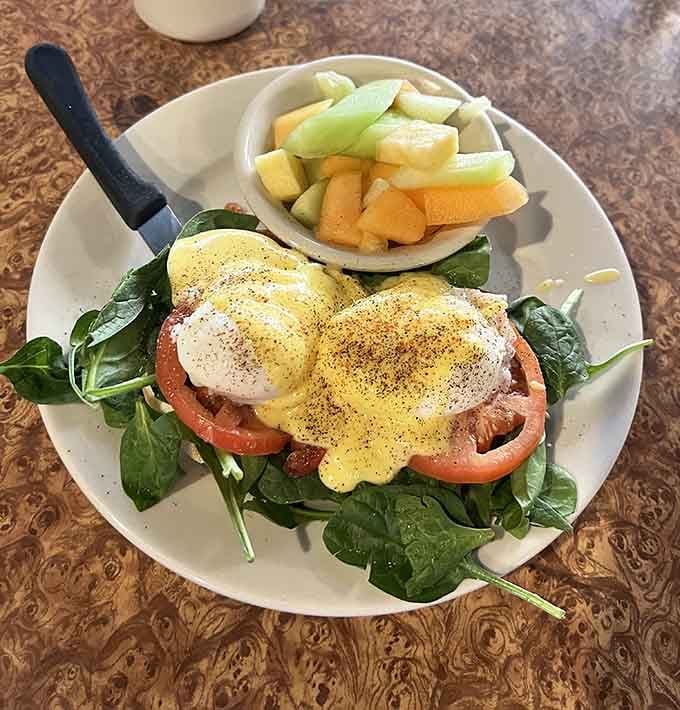 Eggs Benedict done right, with hollandaise that flows like liquid gold over perfectly poached eggs and fresh fruit.