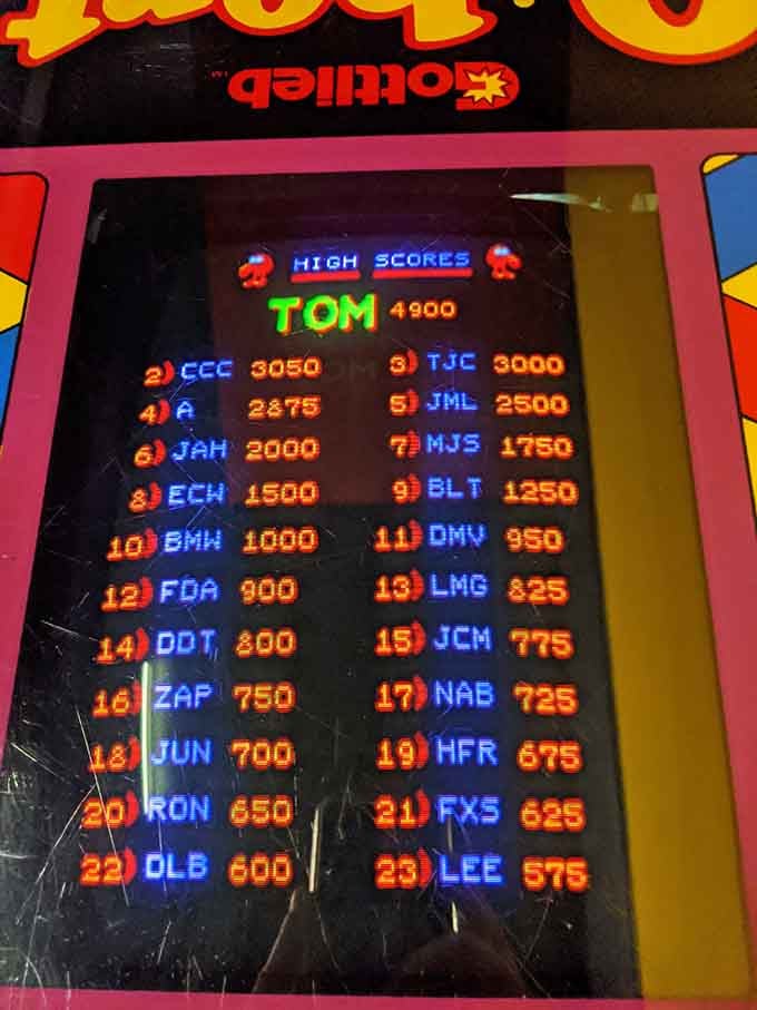 High score boards displaying three-letter legends; digital immortality achieved one quarter at a time, forever preserved in glowing pixels.
