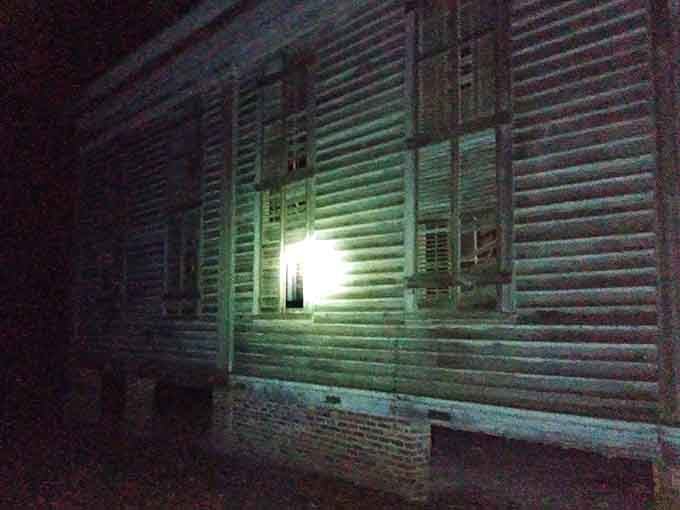 Shuttered windows glow eerily in artificial light, suggesting the building guards secrets better left undisturbed after sunset.