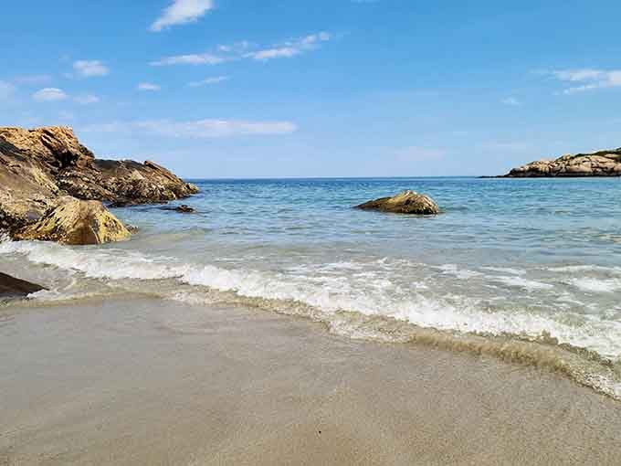 Crystal-clear water laps against smooth rocks in this protected cove, creating a swimming spot that feels like a secret handshake.