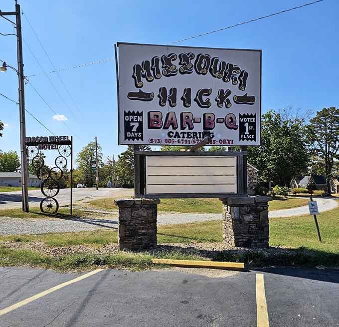 The roadside sign announces barbecue paradise ahead, like a beacon calling hungry travelers home to smoky salvation.