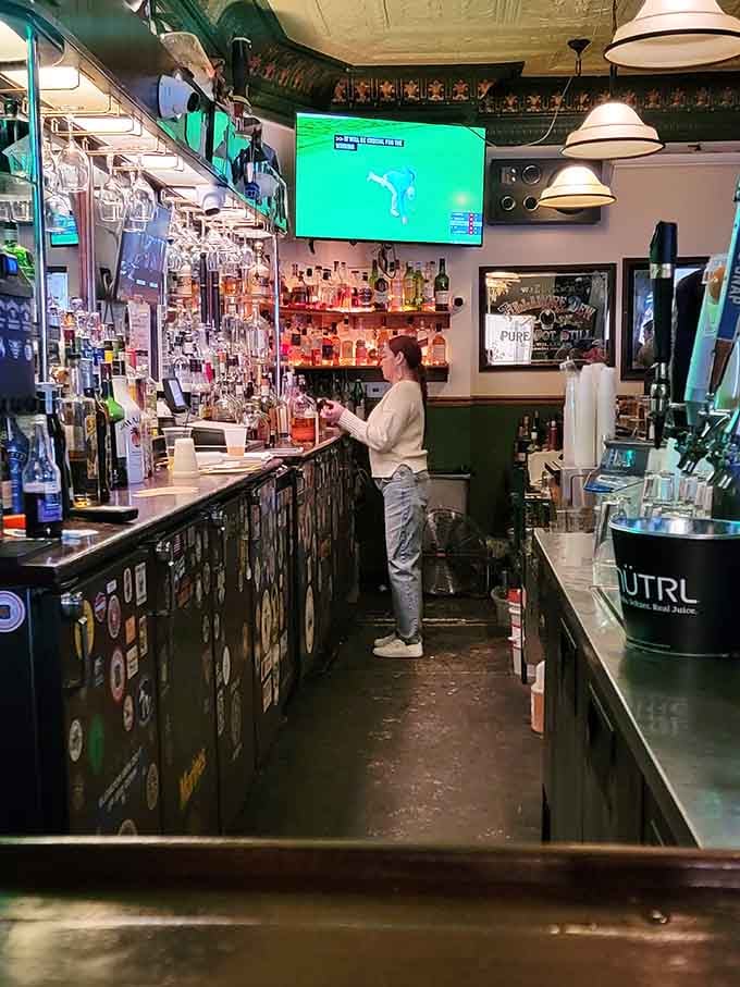 Behind this well-stocked bar, bottles gleam like jewels while a bartender works her magic beneath vintage fixtures and watchful spirits.