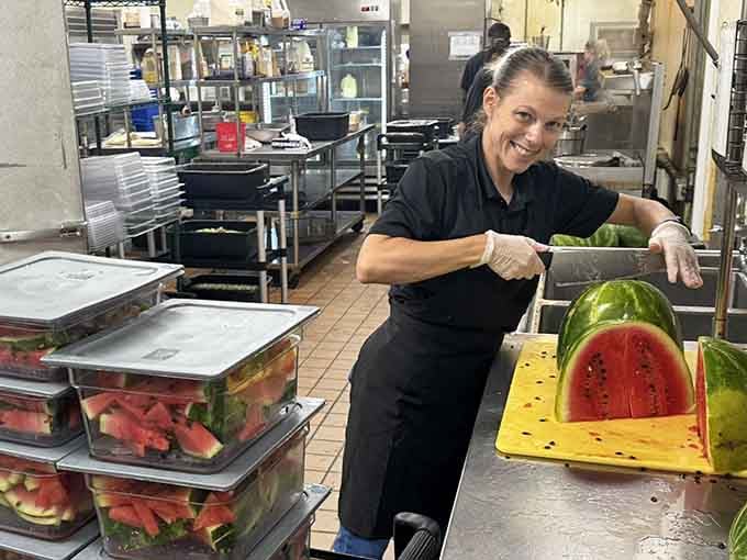Behind every great buffet is someone who cares, slicing watermelon with a smile that says hospitality matters here.
